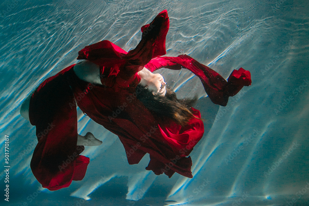 Attractive red-haired young woman swims beautifully underwater in a red ...