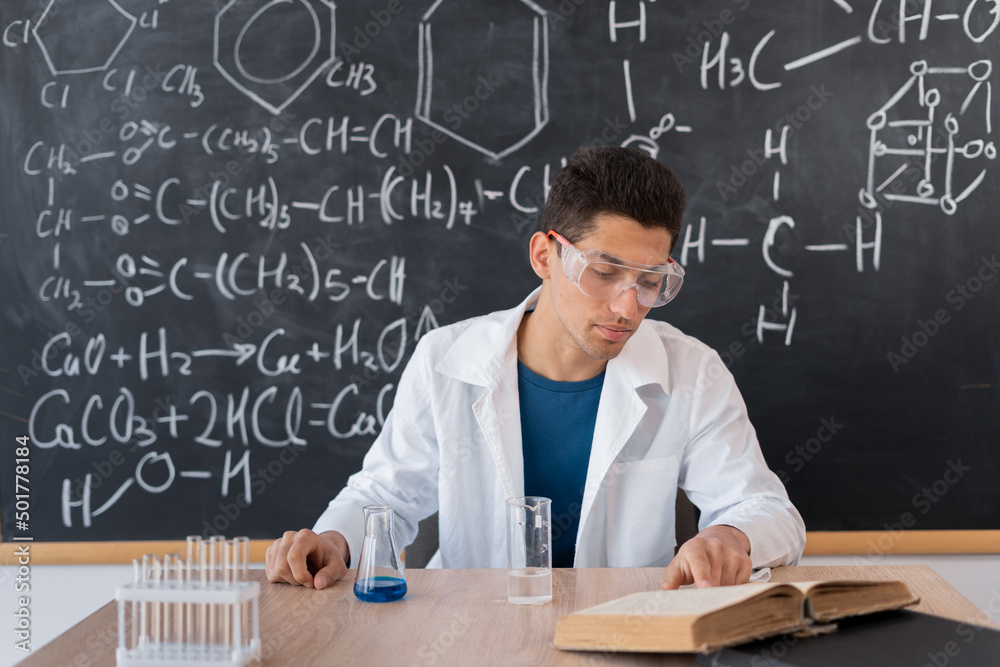 Young male chemistry teacher on blackboard background with chemical ...