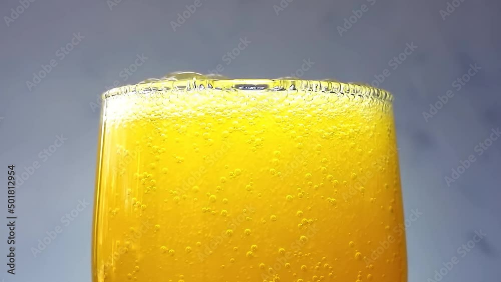 Orange soda is pouring into a glass close-up on a grey background ...