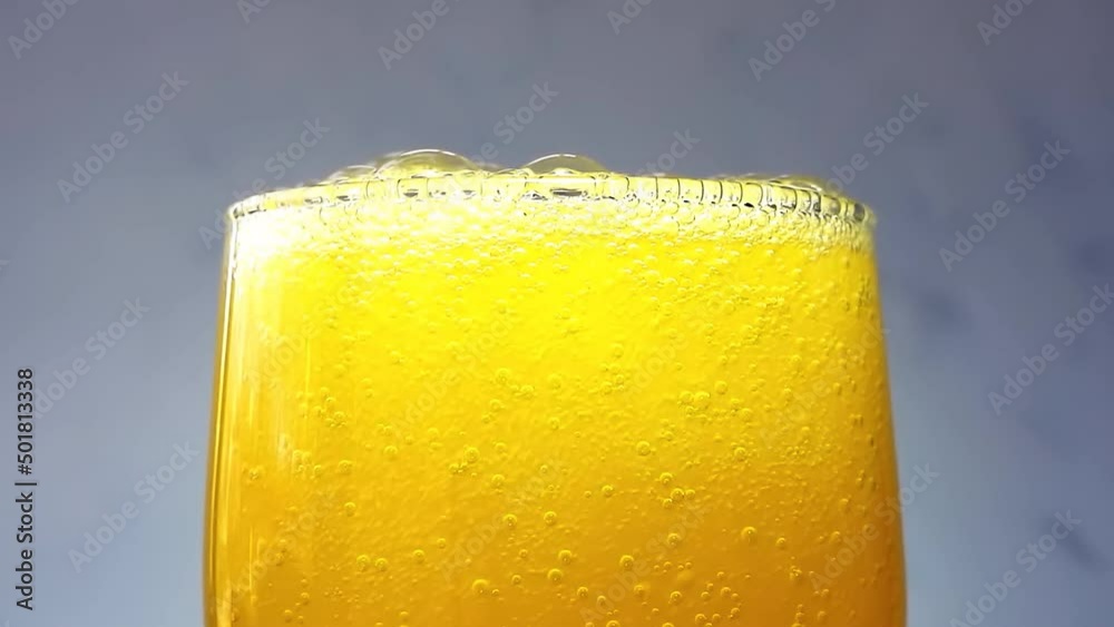 Orange soda is pouring into a glass close-up on a grey background ...