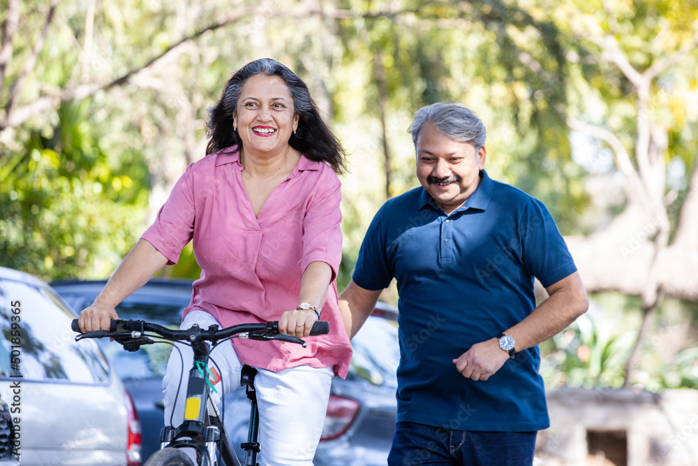 Happy Indian Senior couple riding bicycle in the park summer, active old age people and ...