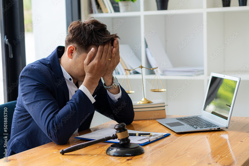 An anxious young Asian lawyer covers his face and works on paper and ...