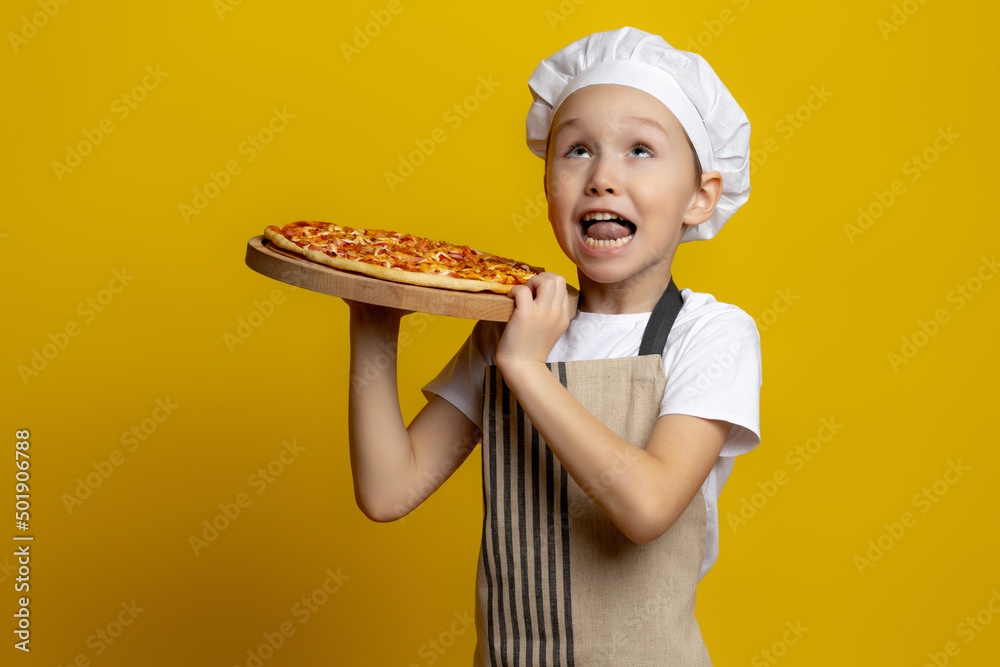 Beautiful cute chef boy in an apron and a chef's hat holds a pizza tray ...