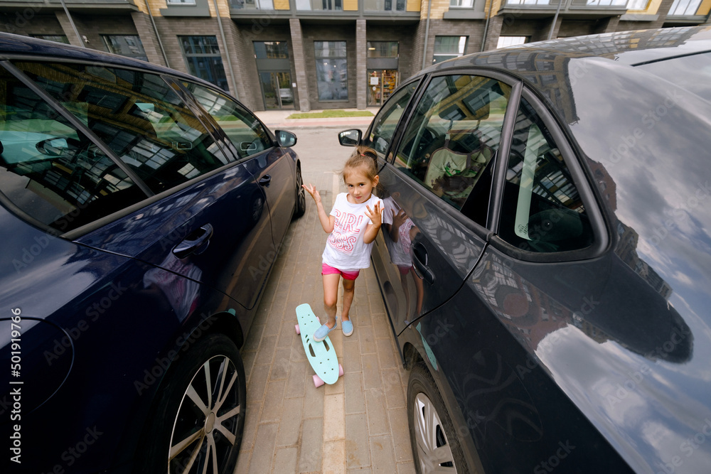 Girl on skateboard stands between cars on the roadway and raises hands ...
