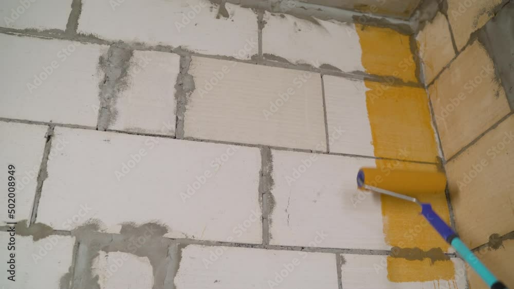 A hand with a roller primes the sanded wall with a mortar during the ...