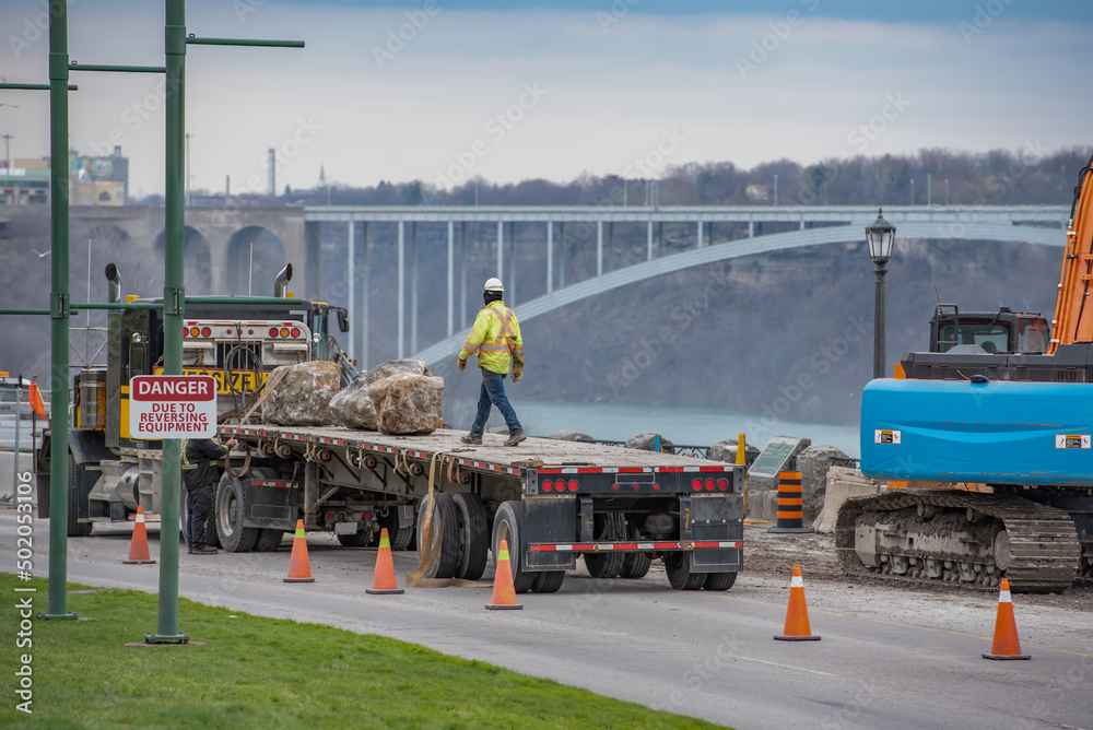 Construction worker on back of a semi truck with flatbed trailer loaded ...
