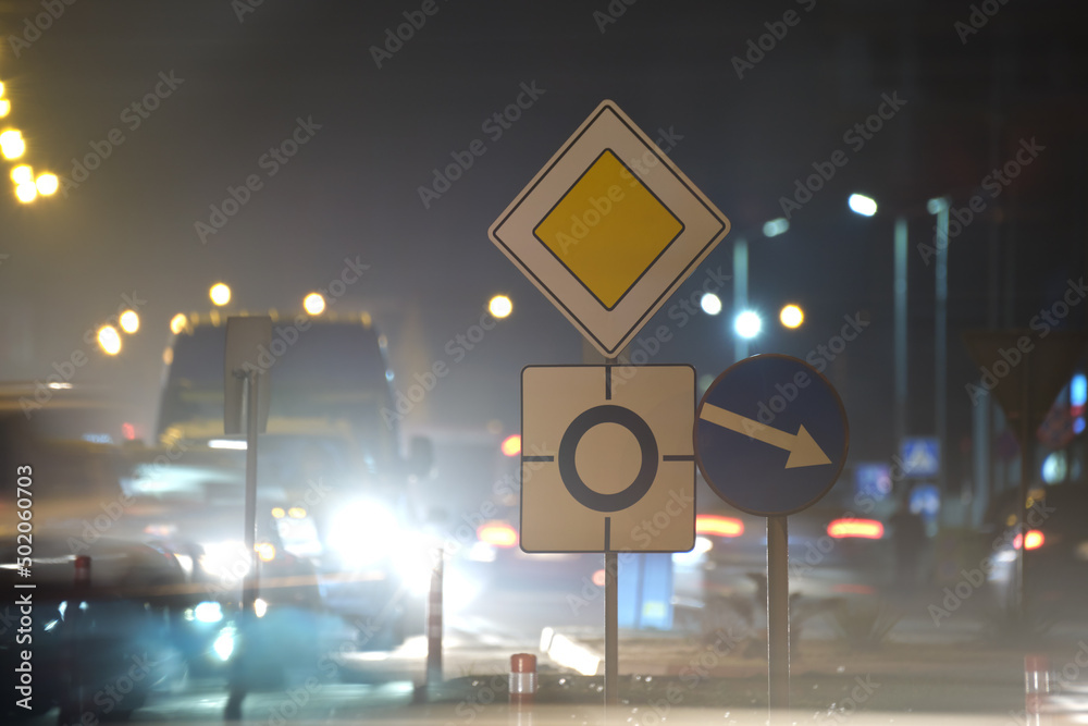 Roundabout road signs with blurred cars on city street traffic at night ...