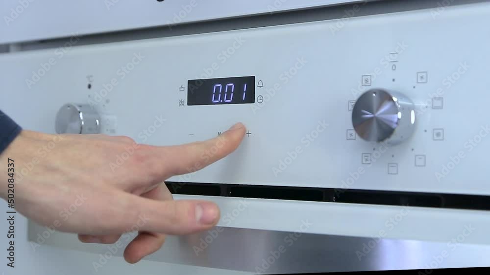 Person hand touching sensor button on electric oven in kitchen. Man ...