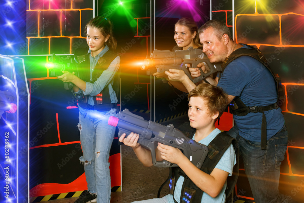 glad young parents and children with laser pistols playing laser tag in ...