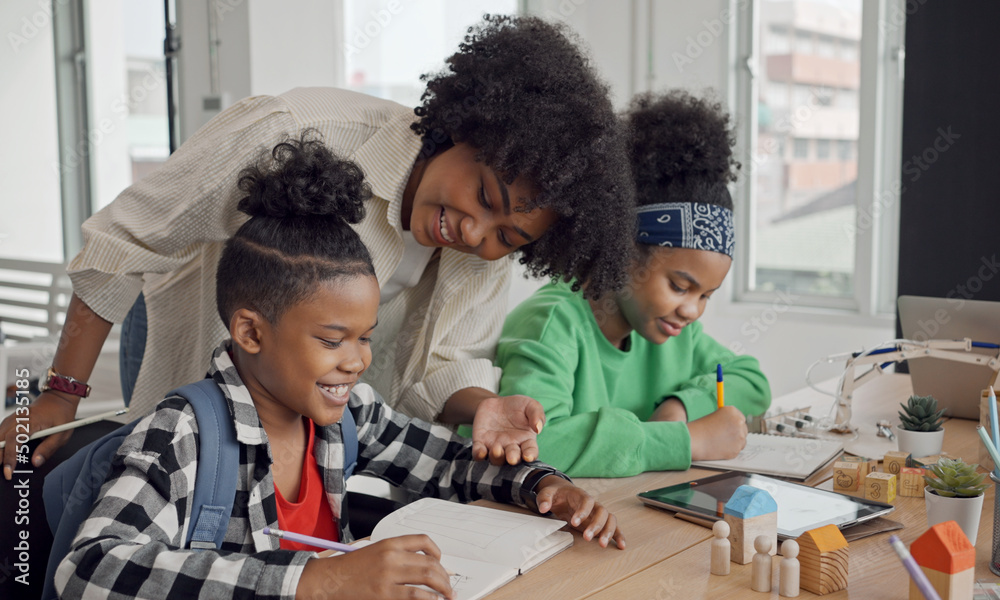 African American female teacher standing with pupils teaching writing ...