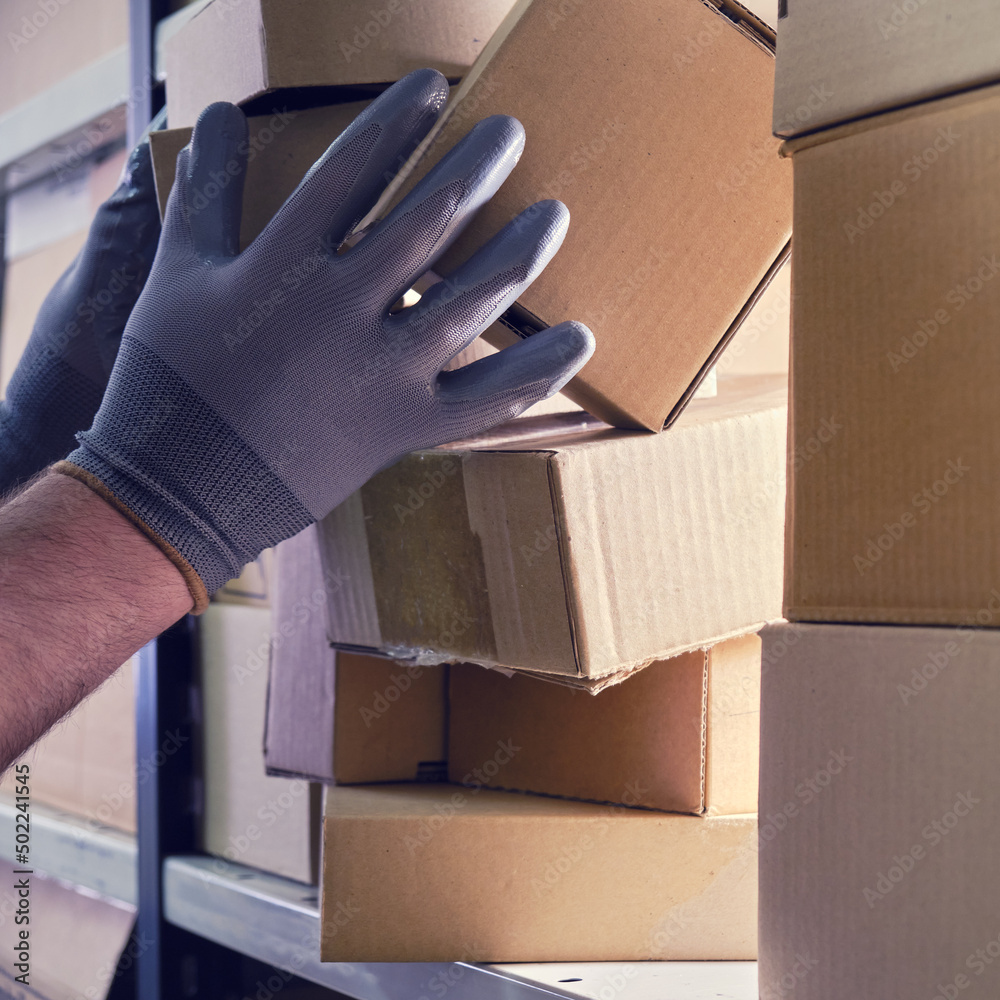 A worker man hands hold cardboard boxes on the shelves of a fully ...