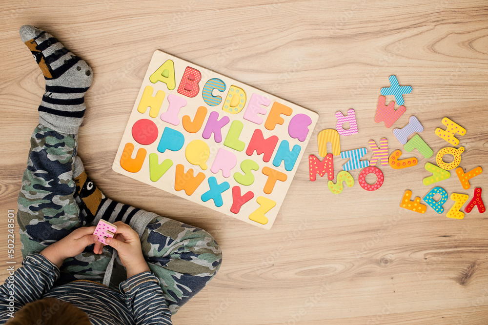 Two year boy playing with wooden alphabet letters board on the floor ...