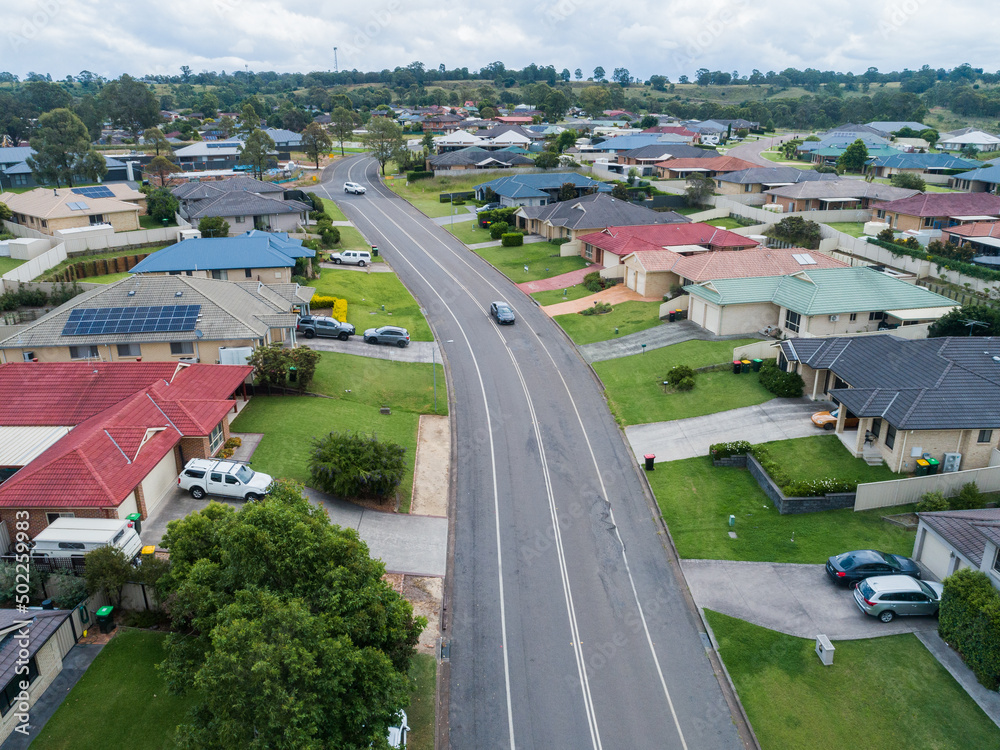 Car driving down street in residential area with houses and cars parked ...