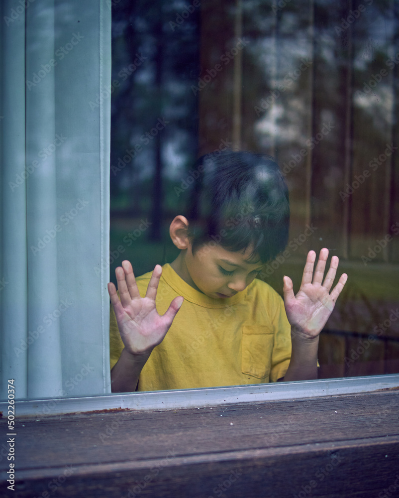 Alone latino child leaning his hands behind the glass of the window ...