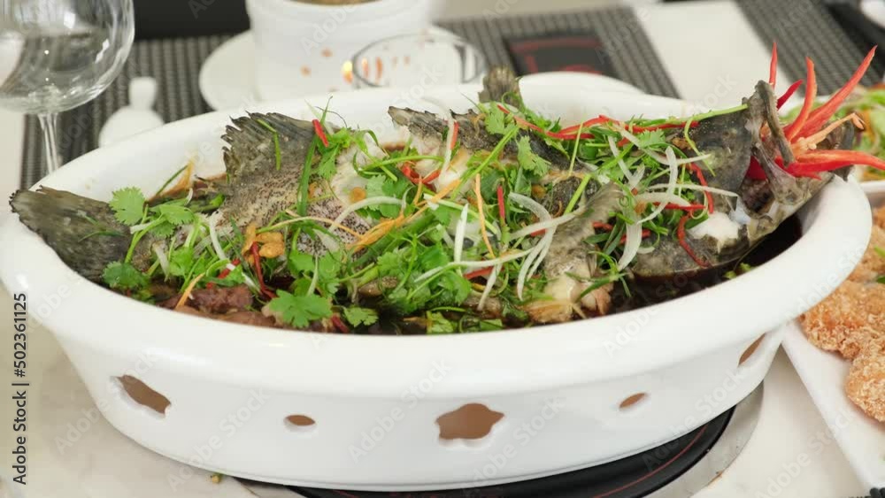 Closeup footage of a steam grouper fish served in a white plate in the ...