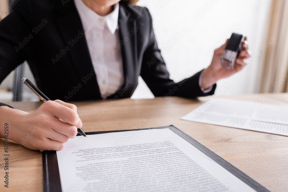 partial view of notary signing contract and holding stamper on blurred ...