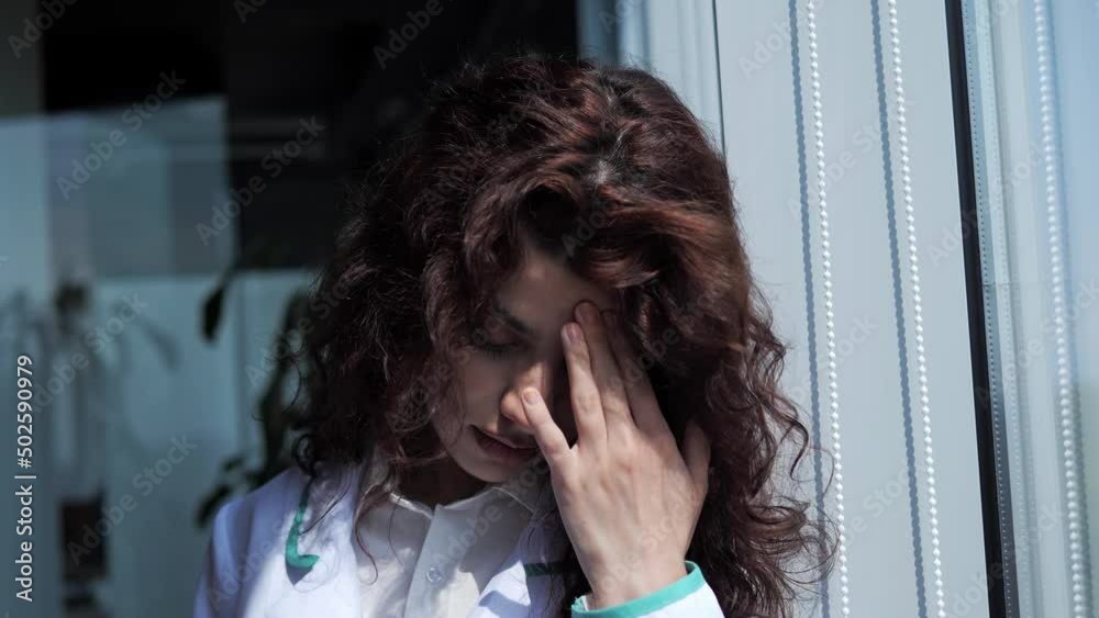 Tired woman doctor intern with curly hair looking through the window ...