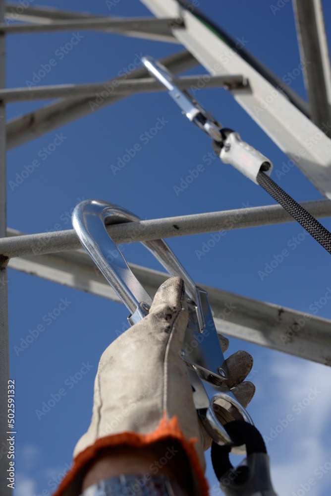 Concept: Work at height. Detail of a gloved hand anchoring a safety ...