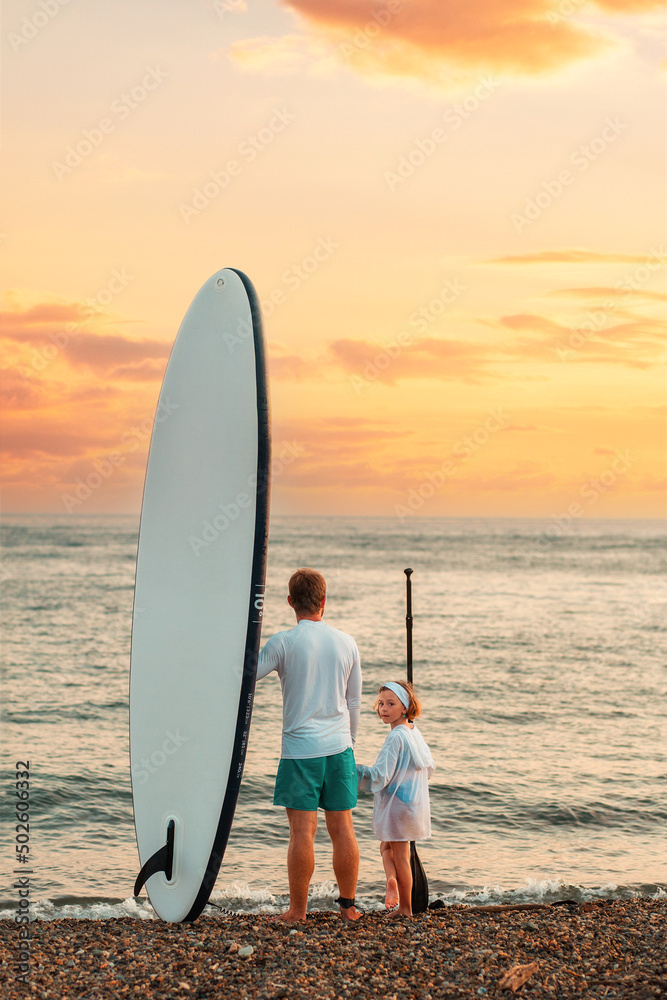 Summer surfing. Father and daughter standing at the beach with a sup ...