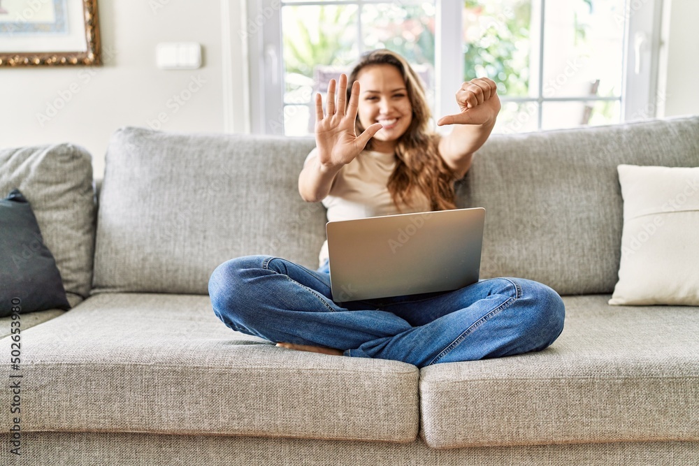 Beautiful young brunette woman sitting on the sofa using computer ...