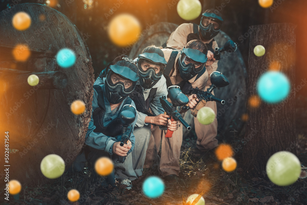 Team of male and female paintball players with marker guns aiming on ...