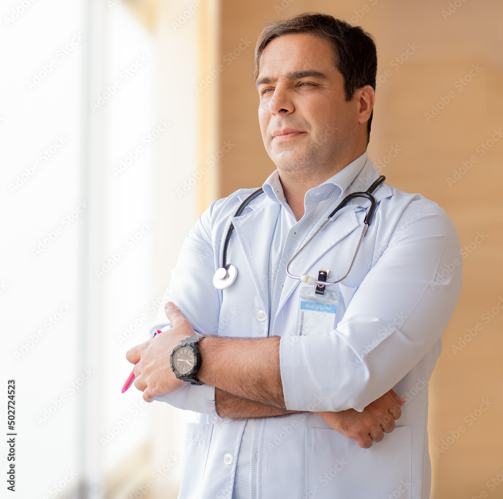 Thoughtful serious male doctor standing by window looking away arms ...