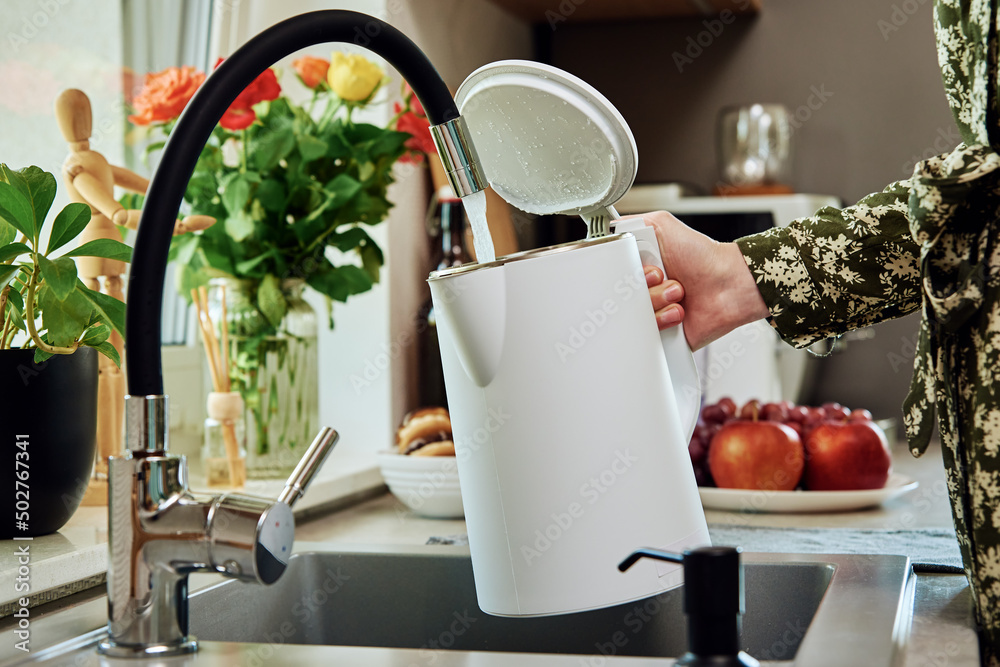 Woman pouring clean filtered water from faucet into electric kettle for ...
