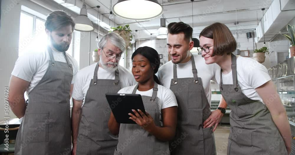 Mixed-races team of cooks standing in restaurant, watching something on ...