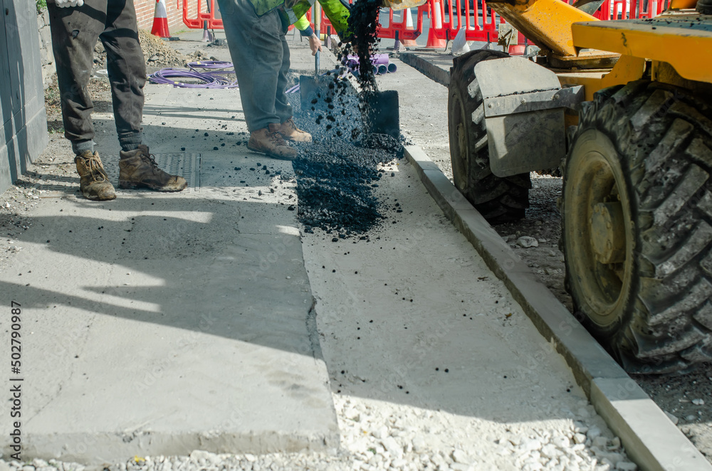 Construction workers placing hot tarmac after installation of new ...