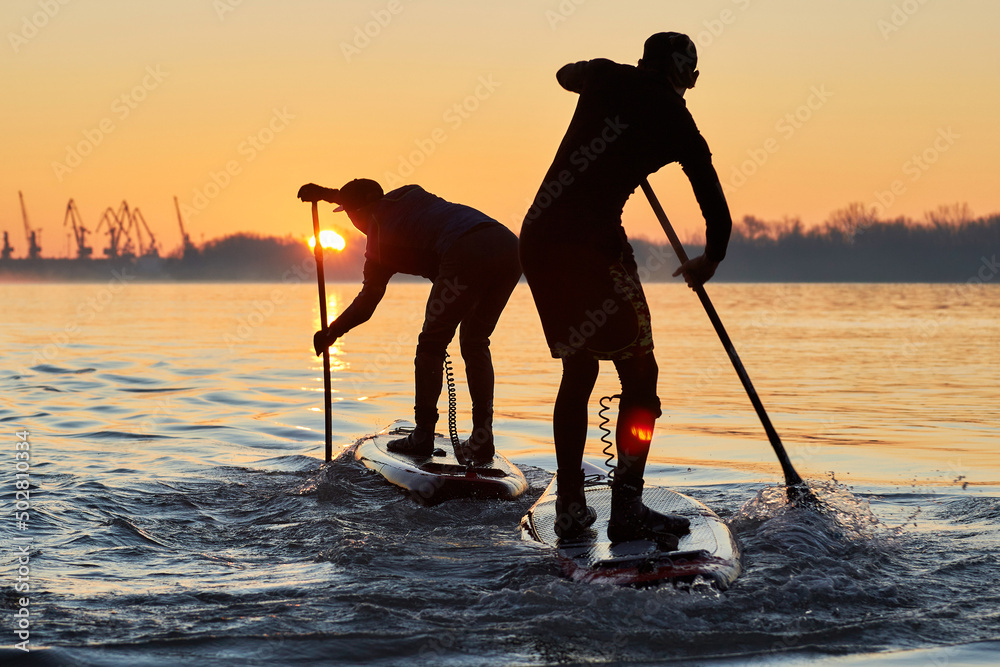 Silhouettes of a two men rowing on stand up paddle boarding (SUP) at ...