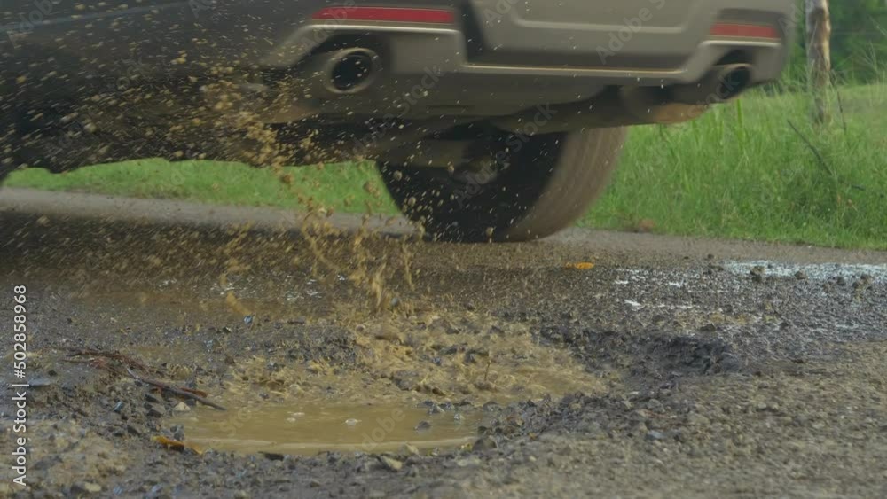 CLOSE UP: Car driving and splashing water from road pit puddle on paved ...