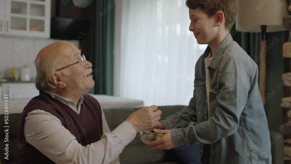 Boy offering candy in bowl to his old grandfather.Little boy offering ...