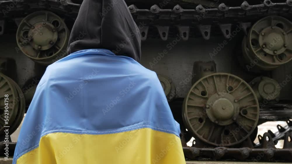 Woman holding Ukrainian flag, with battle tank in background. Russia ...