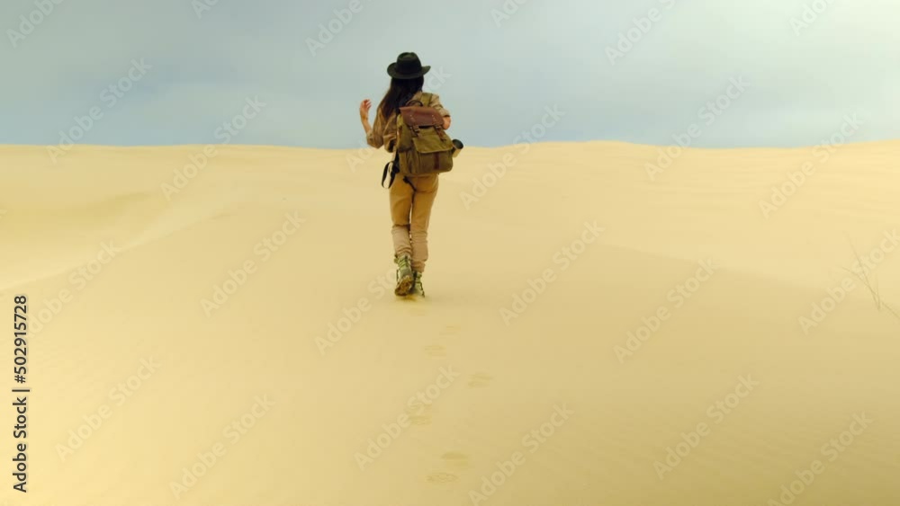 tourist in safari style walks through the sandy desert, leaving ...