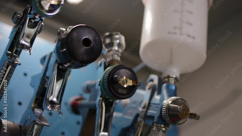 four spray guns in cabinet. High-precision airbrushes hang next to ...