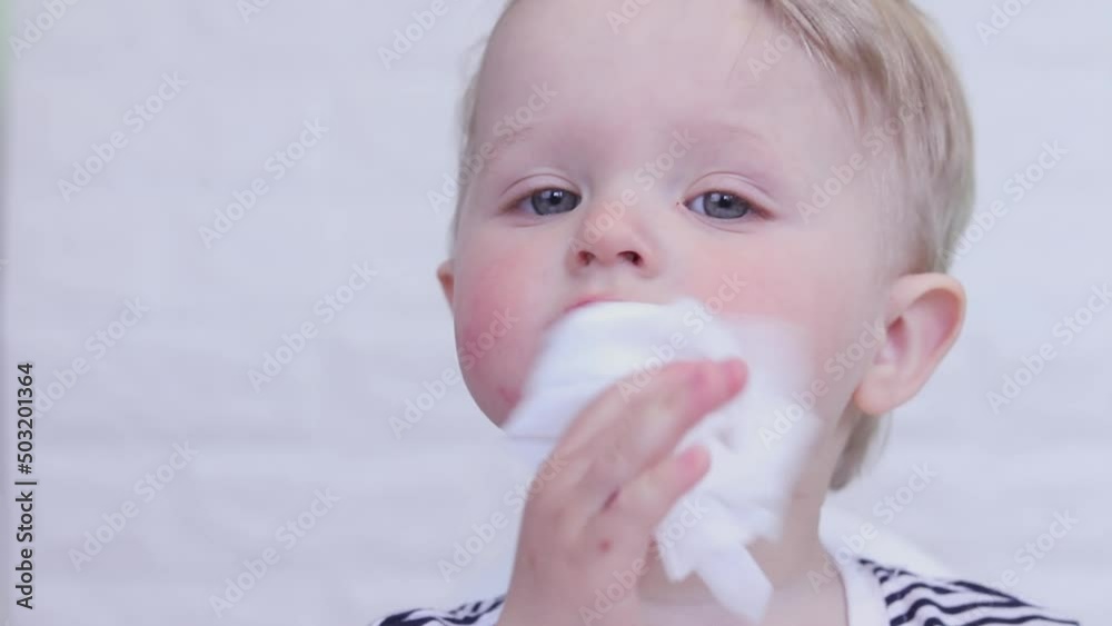 The kid wipes his dirty face with a white napkin after eating. Smiling ...