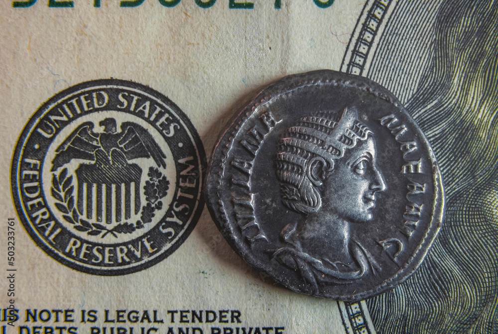 An old Roman coin lies on a 100 dollar bill near the badge with an ...