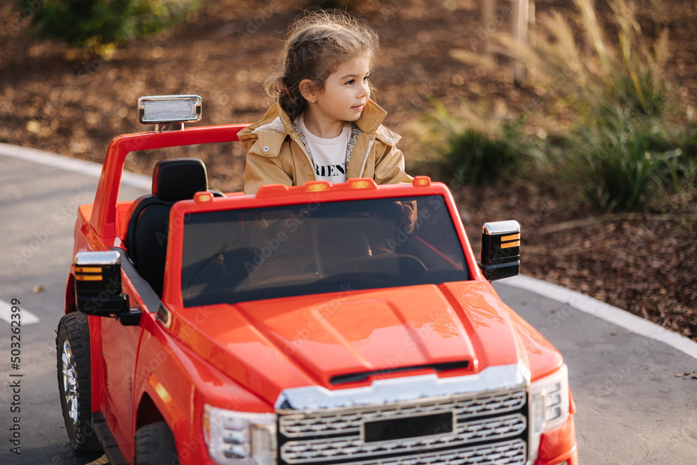 Cute little girl rides in a mini city on a red electric car jeep ...