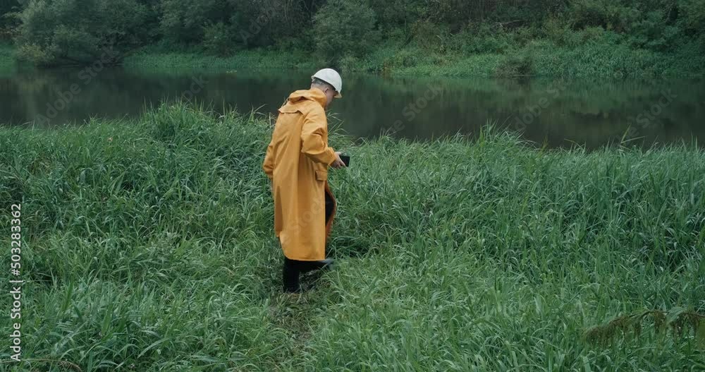 Construction engineer in protective helmet and yellow raincoat walks to ...
