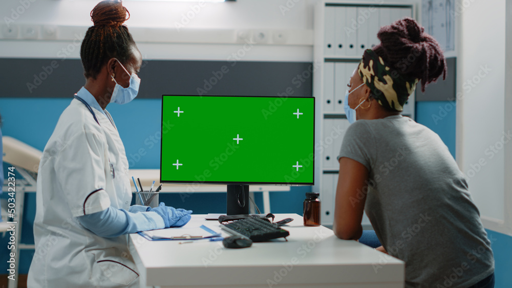 Patient and medic looking at horizontal green screen on monitor at desk ...