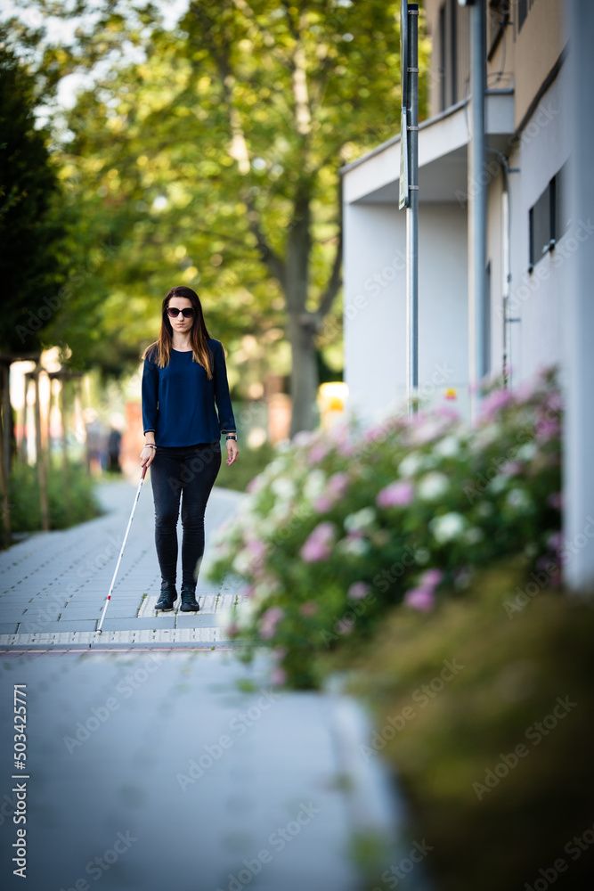 Blind woman walking on city streets, using her white cane to navigate ...
