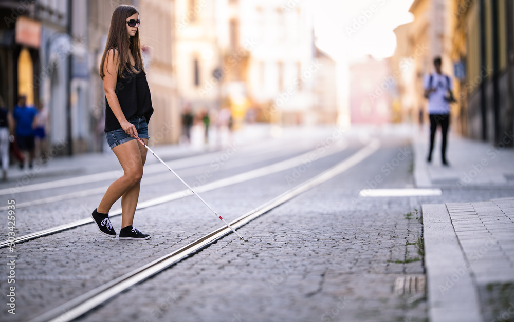 Blind woman walking on city streets, using her white cane to navigate ...