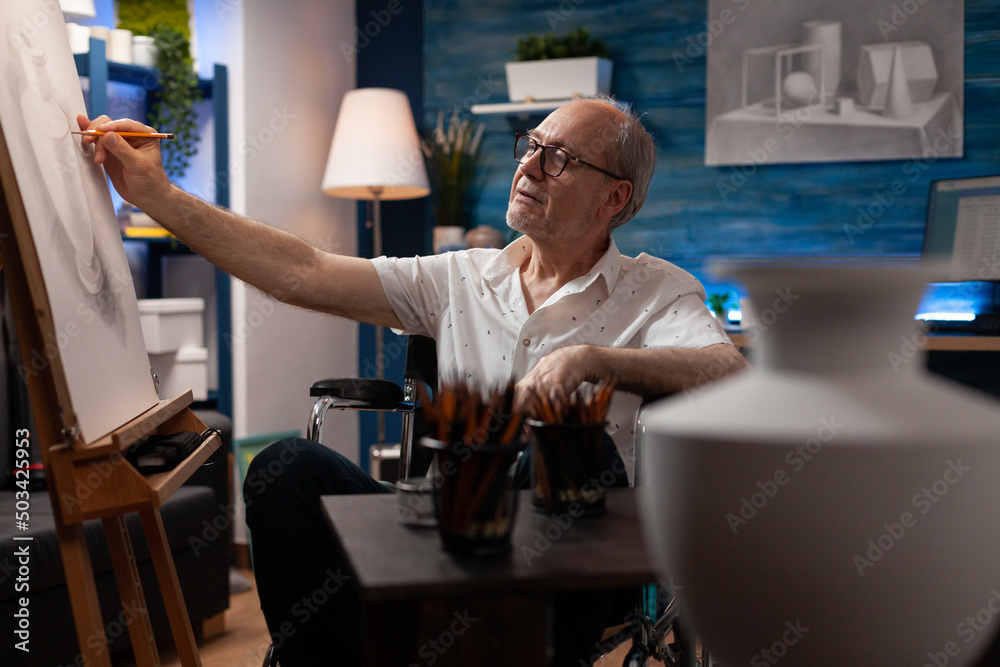 Senior man retired artist using wheelchair doing pencil sketch of vase ...