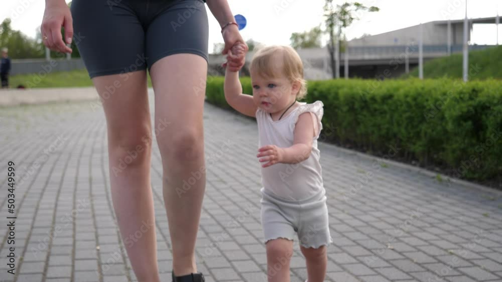 Small baby child toddler baby daughter walks holding her mother hand ...