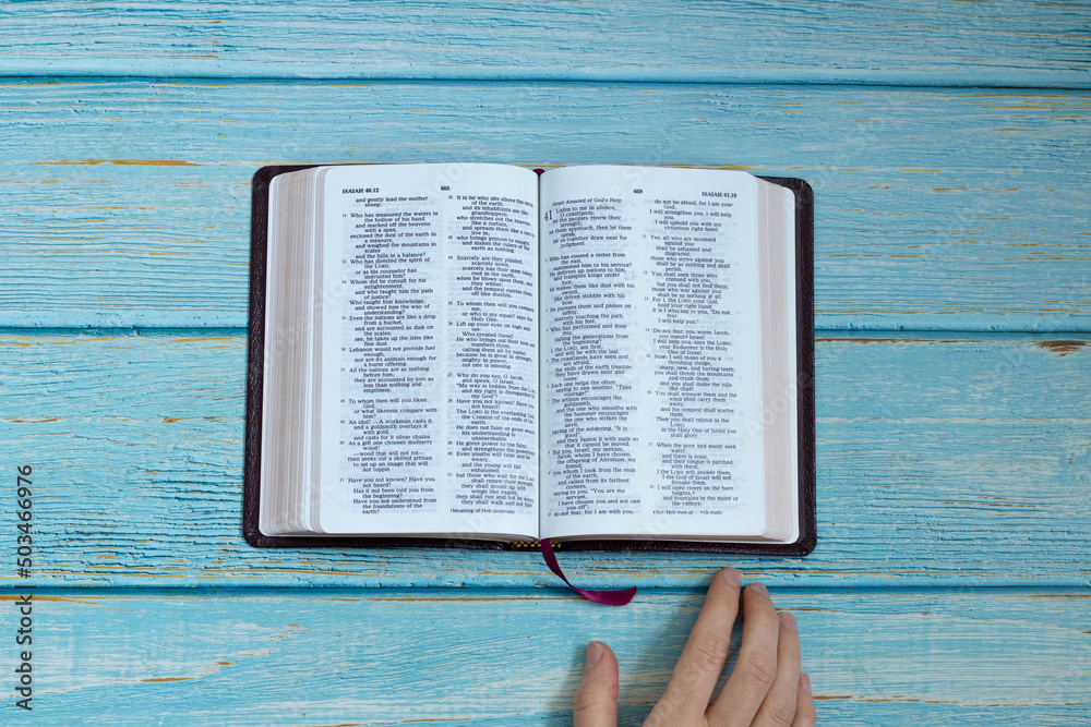 Open Holy Bible Book with hand isolated on a light blue wooden table ...