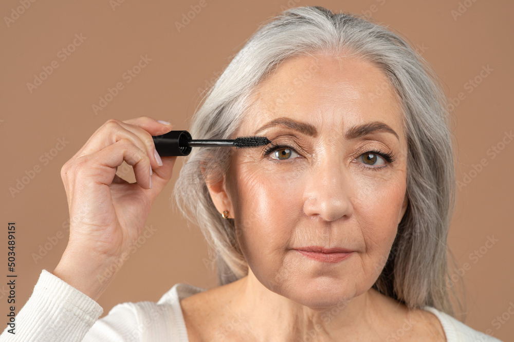 Beauty portrait of charming senior woman applying mascara on her lashes ...