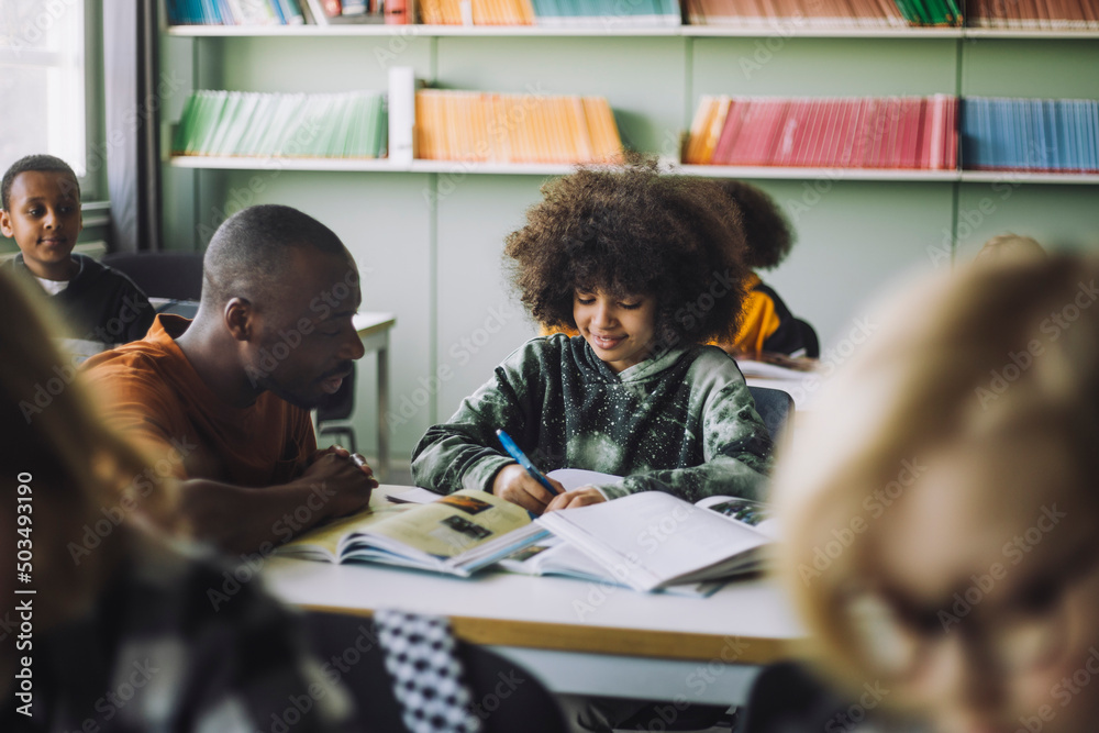Male teacher assisting boy studying at desk in classroom Stock Photo ...