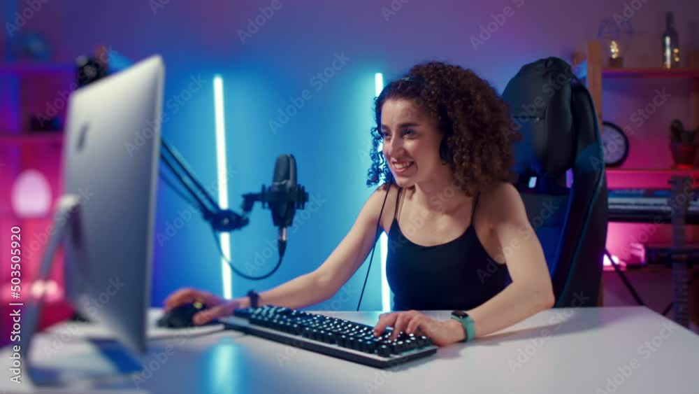 Young woman wearing headphones playing computer game neon fashion room ...