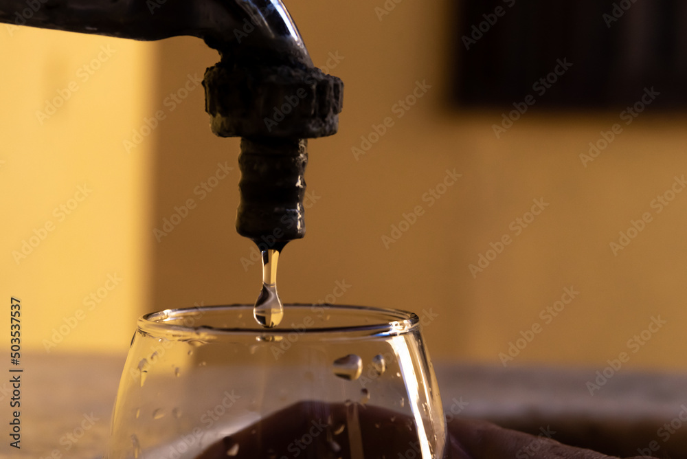 faucet with the last drop of water entering a glass beaker, water ...