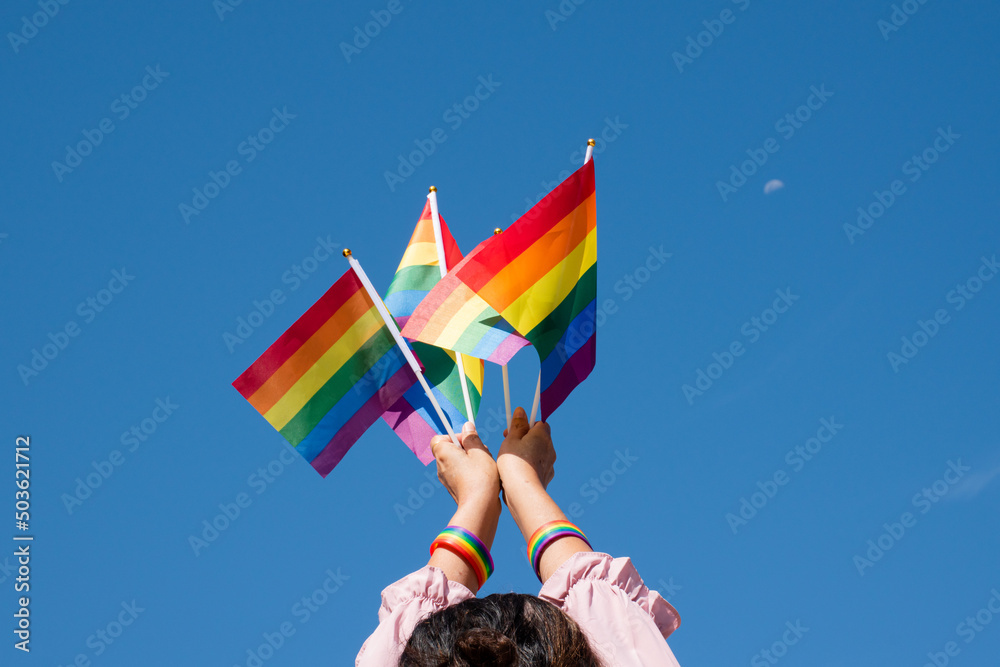 Rainbow flags showing in hands against clear bluesky, copy space ...